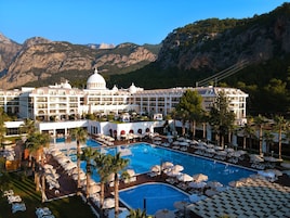 Um resort com uma piscina grande, várias varandas e montanhas ao fundo.