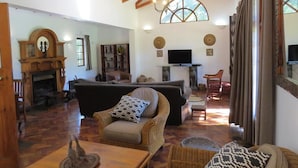 Uma sala de estar ampla com teto alto, vigas de madeira, lareira, televisão e uma grande janela em arco.
