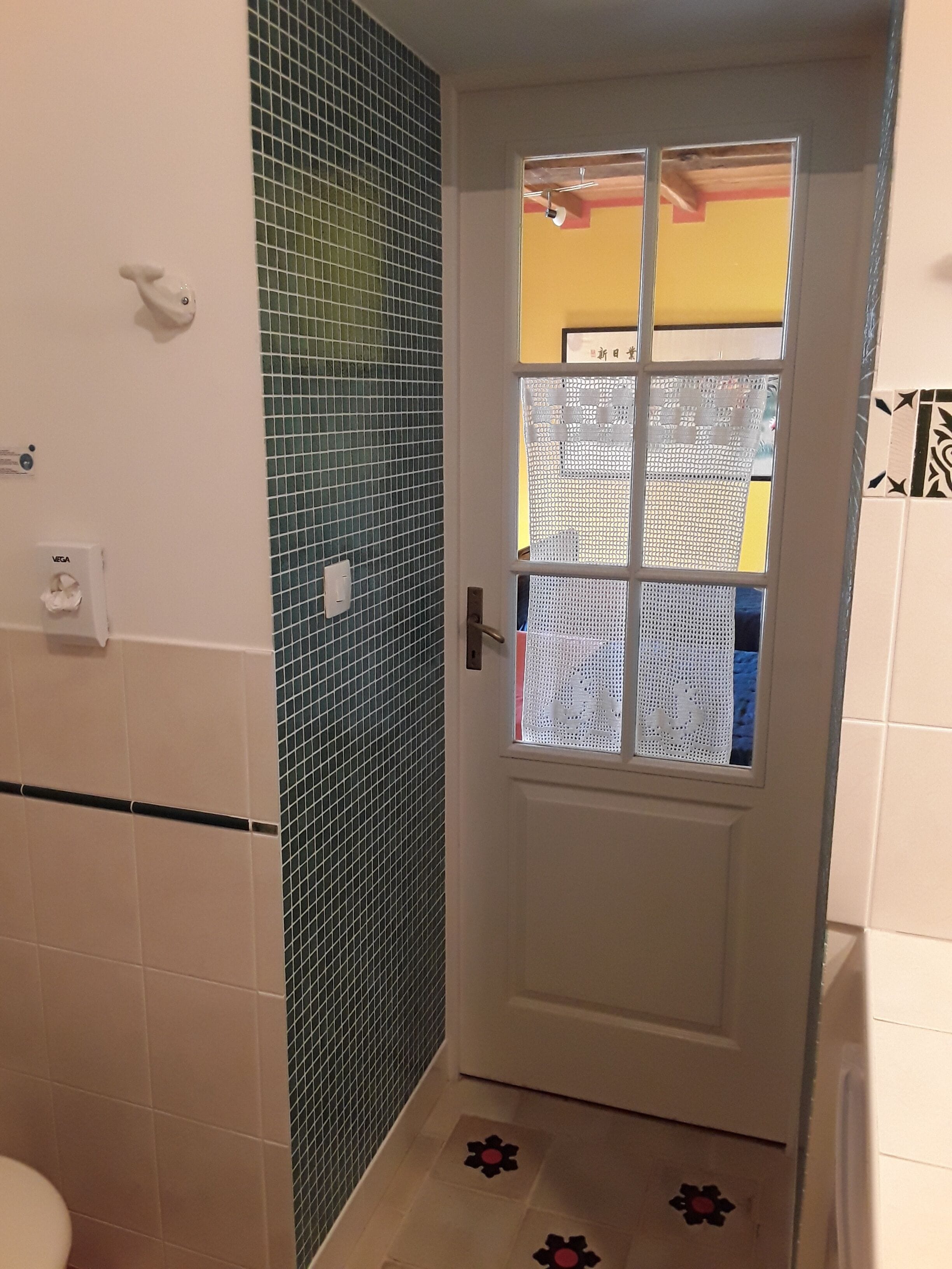 Um banheiro com porta branca, parede revestida de azulejos e vaso sanitário.