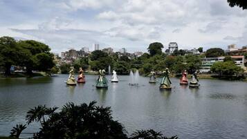 Um parque com estátuas de mulheres vestindo trajes típicos à beira de um lago, rodeado por vegetação e edifícios ao fundo.