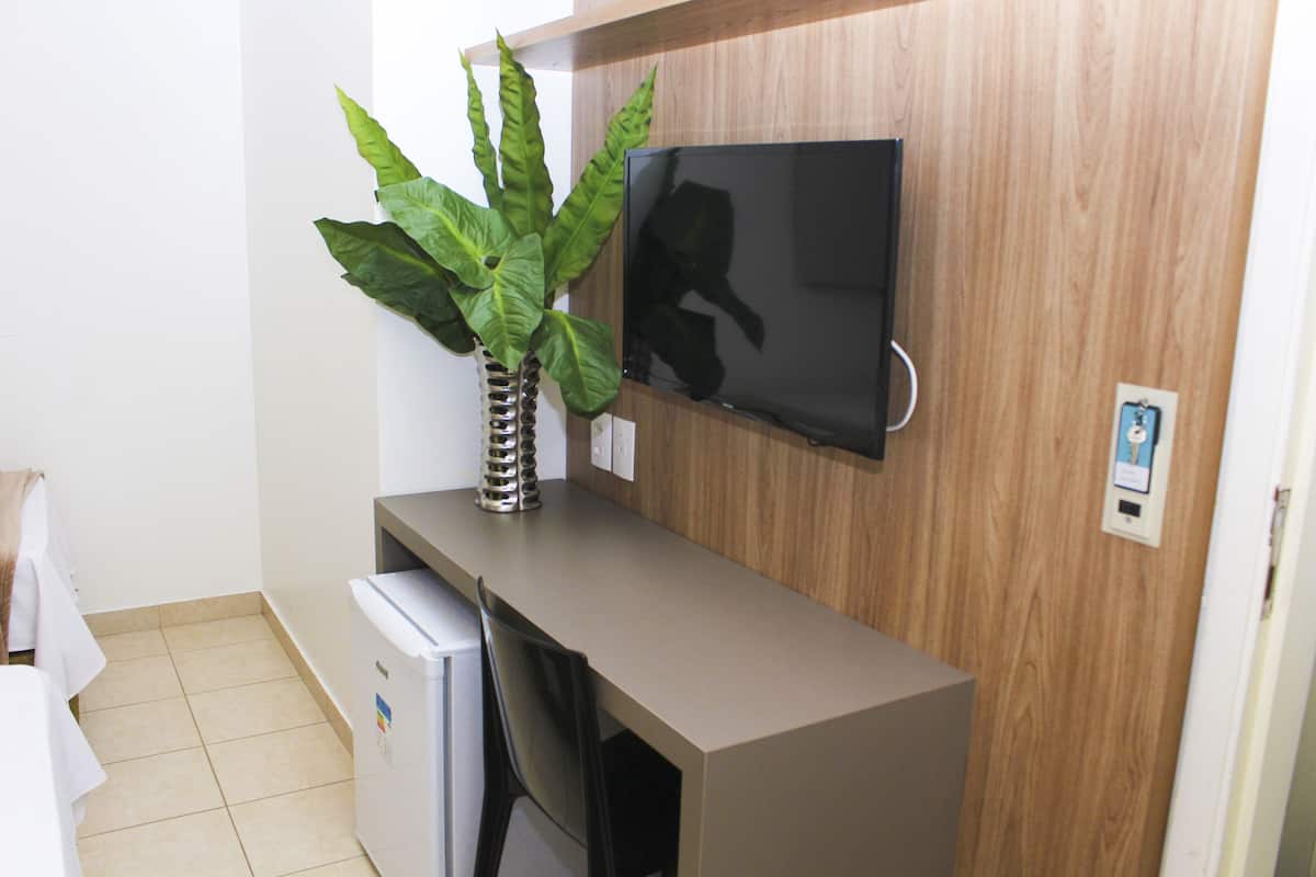 Uma pequena cozinha compacta com geladeira, pia e bancada. Há um vaso de planta na bancada e uma TV de tela plana presa na parede.