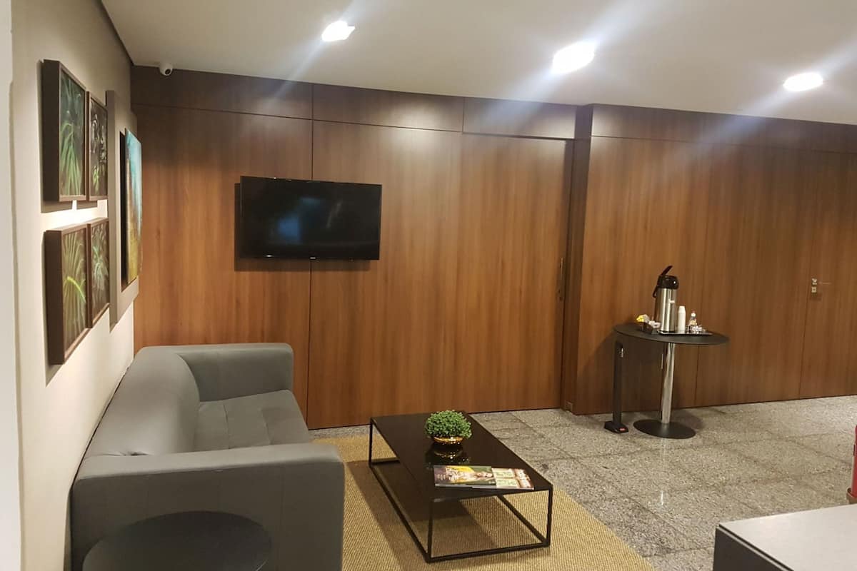 Uma sala de estar moderna com um sofá, uma mesa de centro com uma planta, uma TV fixada na parede e uma pequena mesinha de apoio com uma chaleira.