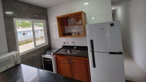 Uma cozinha moderna com armários brancos, uma geladeira de aço inoxidável, micro-ondas, fogão e uma prateleira de madeira sobre a pia.