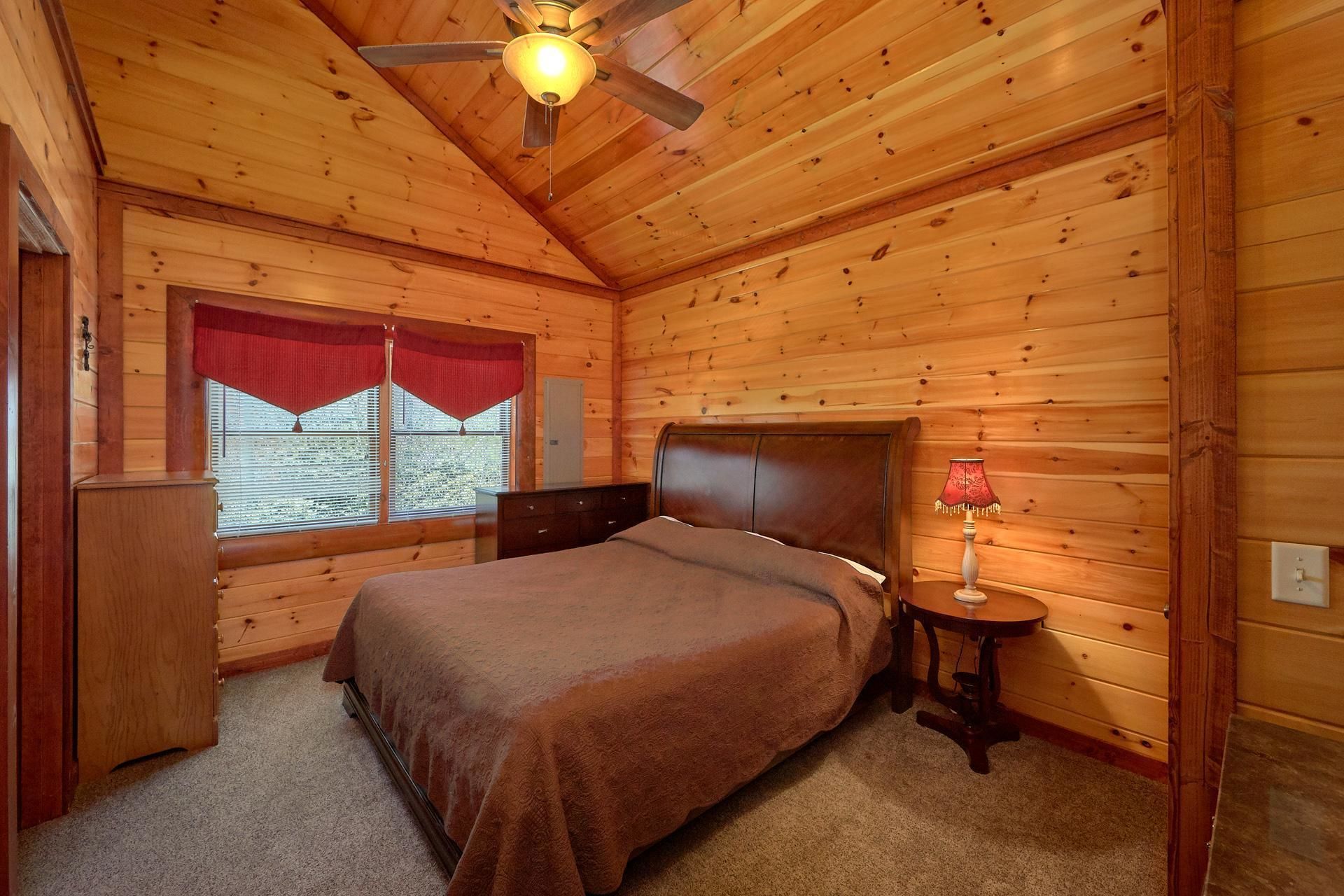 Quarto de cabana de madeira com cama, mesa de cabeceira, luminária e ventilador de teto.