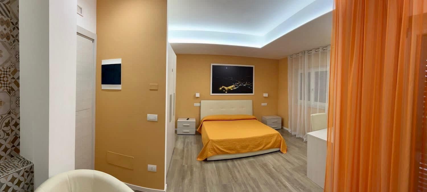 Quarto de hotel com cama, mesas de cabeceira, cortinas numa janela e uma obra de arte na parede.