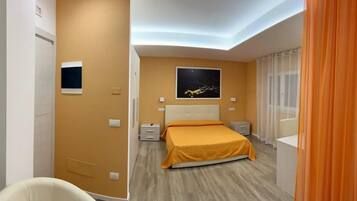 Quarto de hotel com cama, mesas de cabeceira, cortinas numa janela e uma obra de arte na parede.