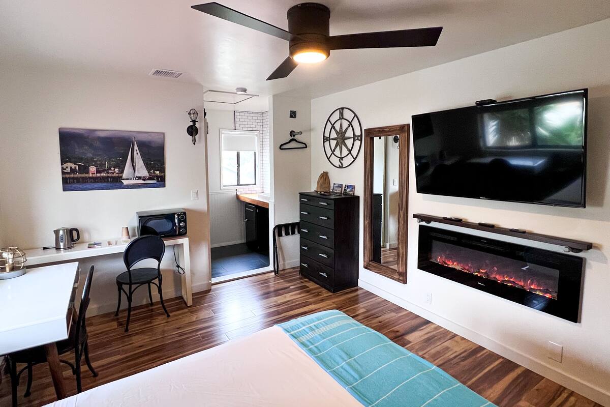 Quarto de hotel com uma cama, uma escrivaninha com computador, televisão, lareira e vista para o exterior.