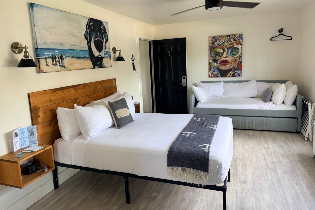 Um quarto com cama, sofá, ventoinha no teto e obras de arte nas paredes.