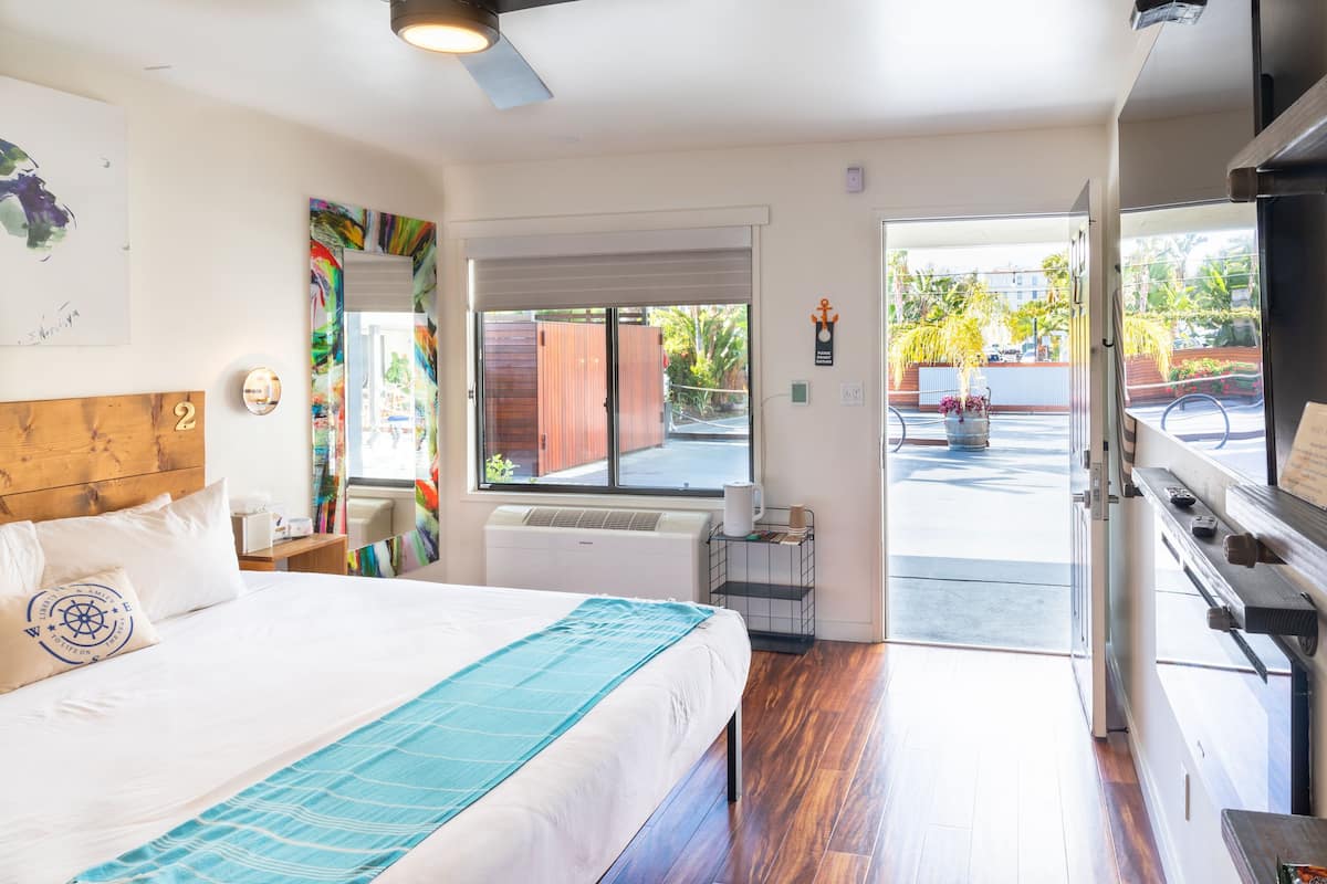 Quarto de hotel com uma cama grande, vista para a área externa, cabeceira de madeira e ventoinha de teto.