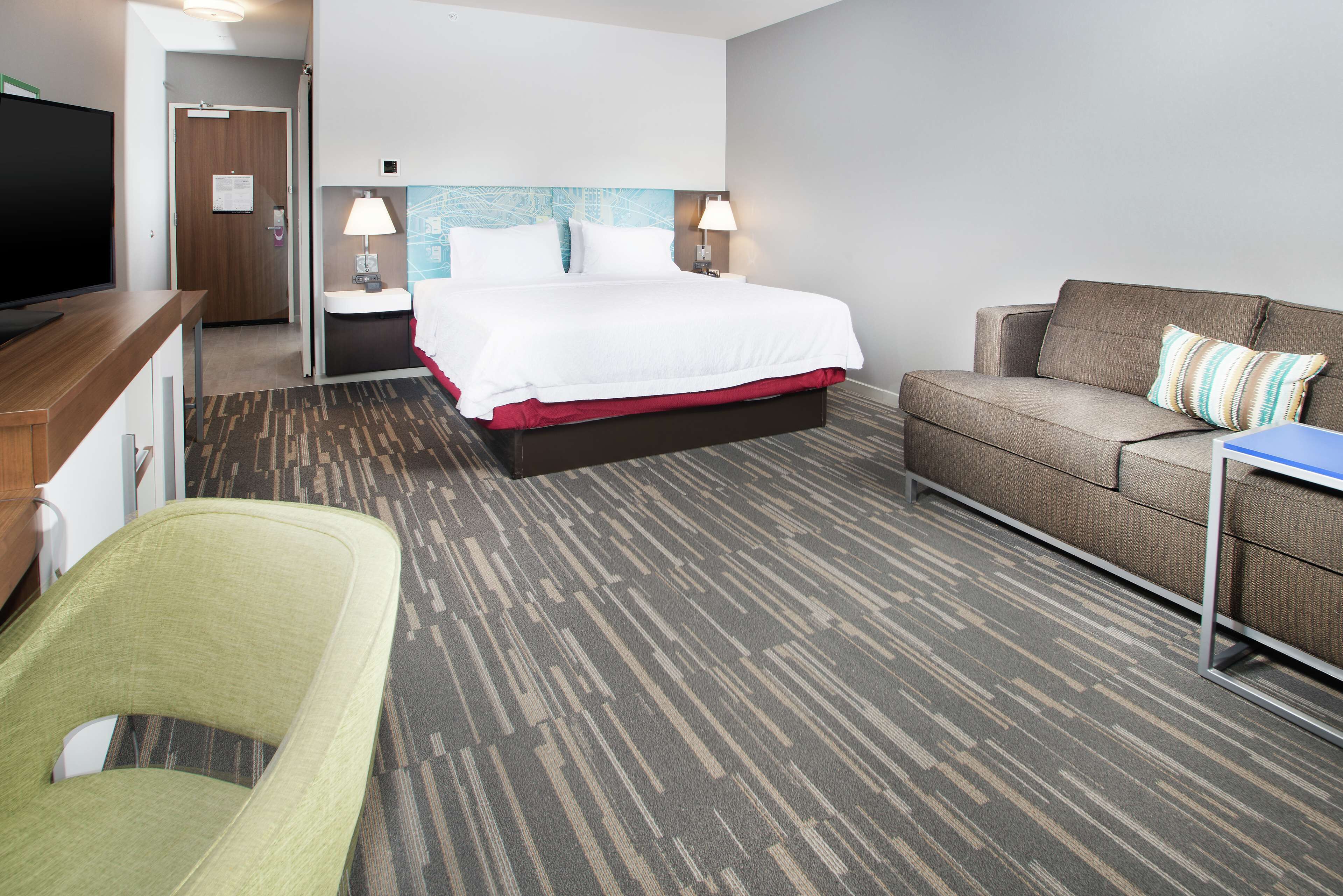 Quarto de hotel com cama, sofá, televisão, escrivaninha e cadeira.