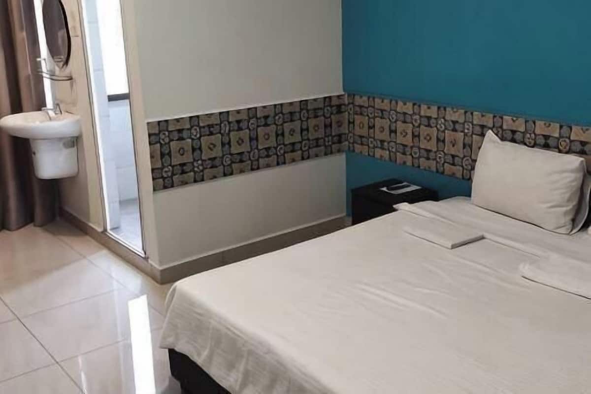 Quarto de hotel com cama, pia, espelho, janela com cortinas e parede revestida de azulejos.