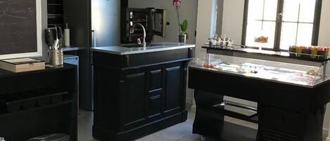 Uma cozinha moderna com armários pretos, geladeira de aço inoxidável, forno embutido e uma vitrine de vidro com alimentos.