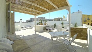 Um terraço no telhado com área de estar coberta, mobiliário de exterior e plantas em vasos.