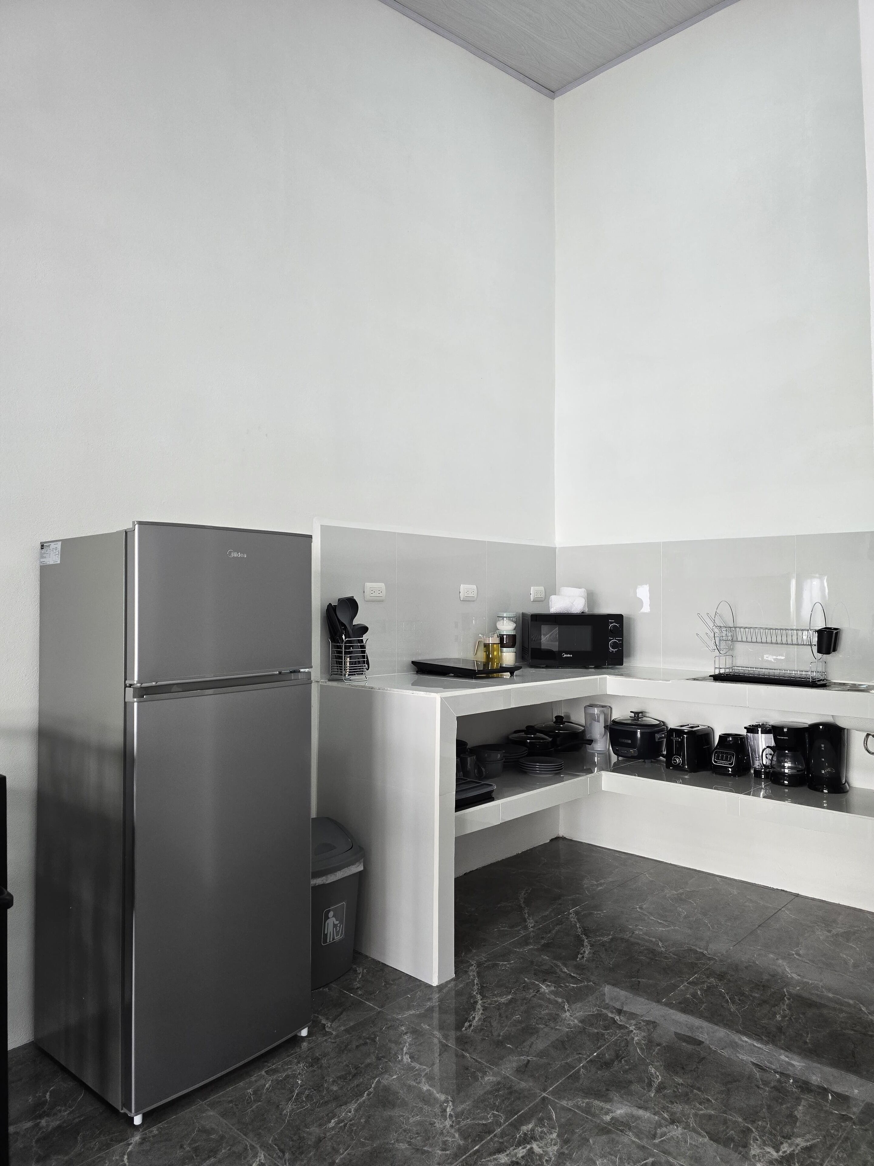 Uma cozinha moderna com geladeira de aço inoxidável, micro-ondas e diversos eletrodomésticos na bancada.