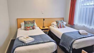 Quarto de hotel com duas camas, cada uma com cabeceira, mesa de cabeceira e abajur.