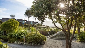 Um jardim com um caminho de cascalho, uma escadaria de madeira e diversas plantas.