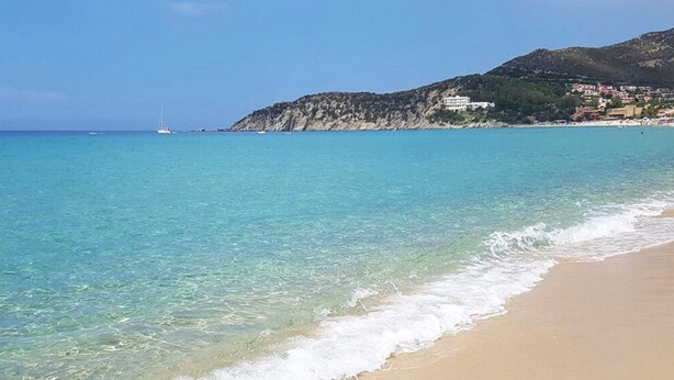 Uma praia com águas turquesa cristalinas, areia dourada e montanhas ao fundo.