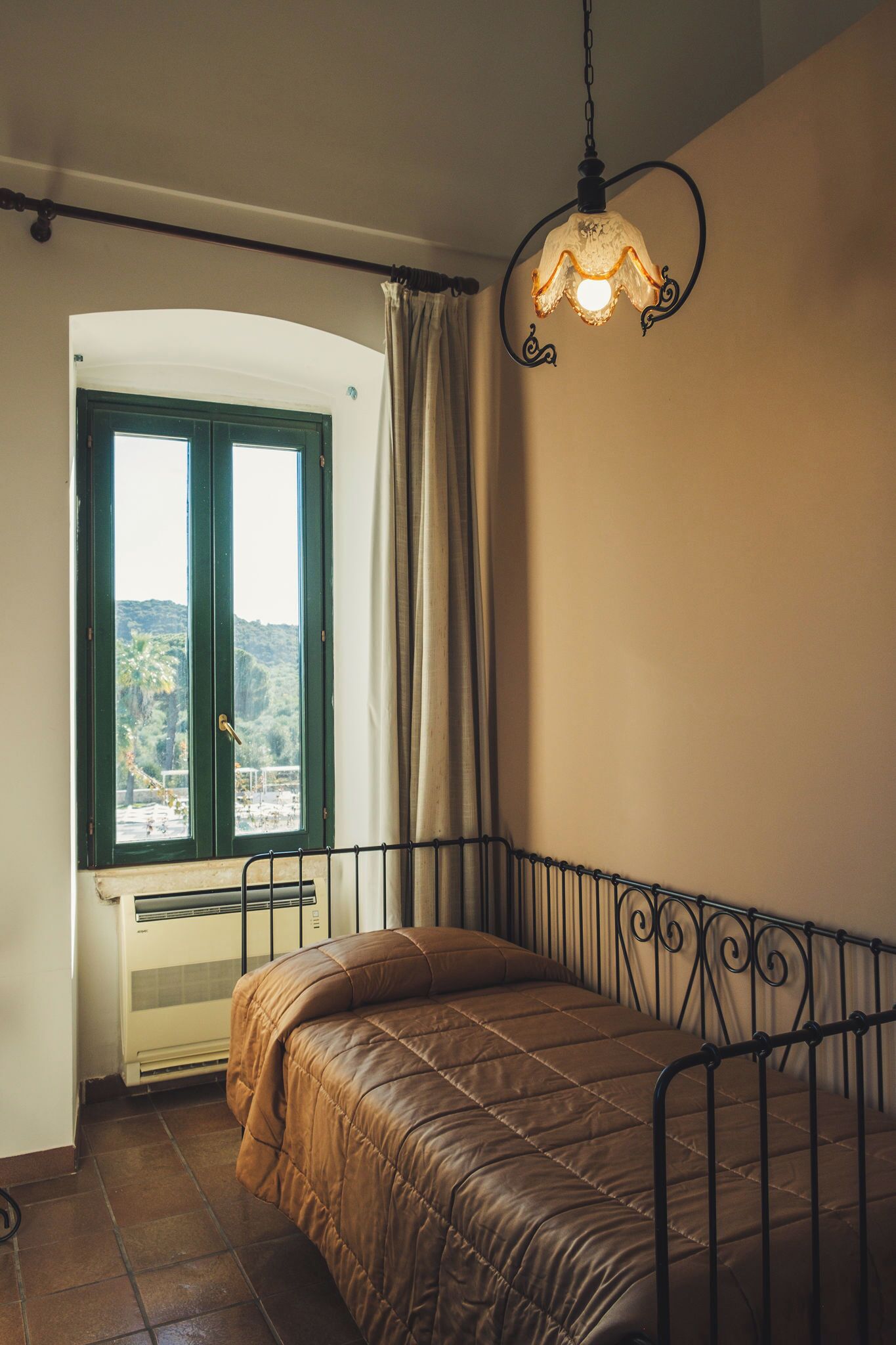Quarto com cama, janela com cortinas e luminária pendente.