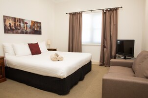 Quarto de hotel com uma cama grande, televisão, sofá e um quadro na parede.