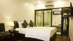 Quarto de hotel com cama, mesa de cabeceira com luminária, telefone e pequena mesa com chaleira.