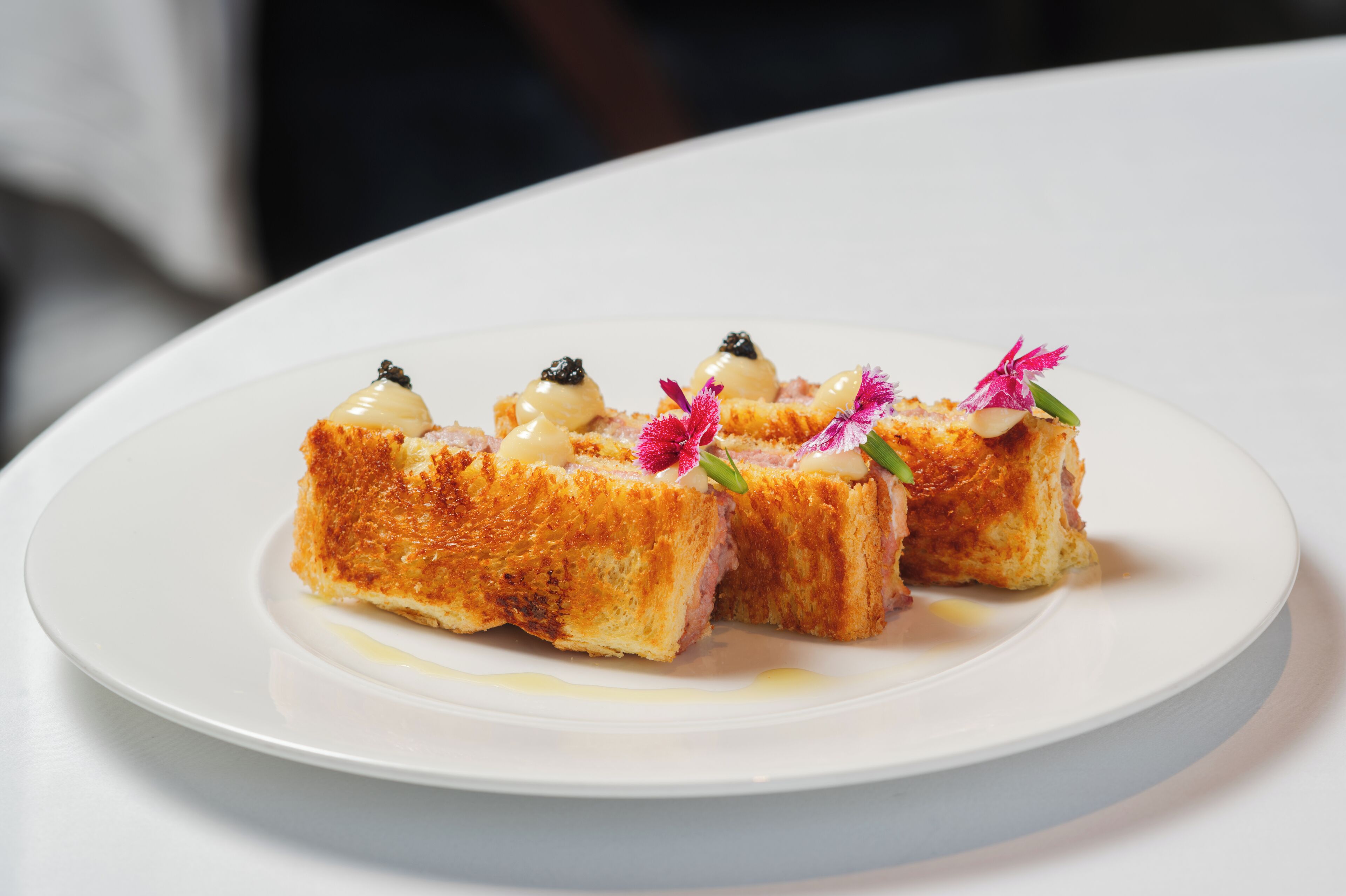 Um prato branco com três porções de comida, cada uma decorada com uma flor e um pequeno objeto preto.