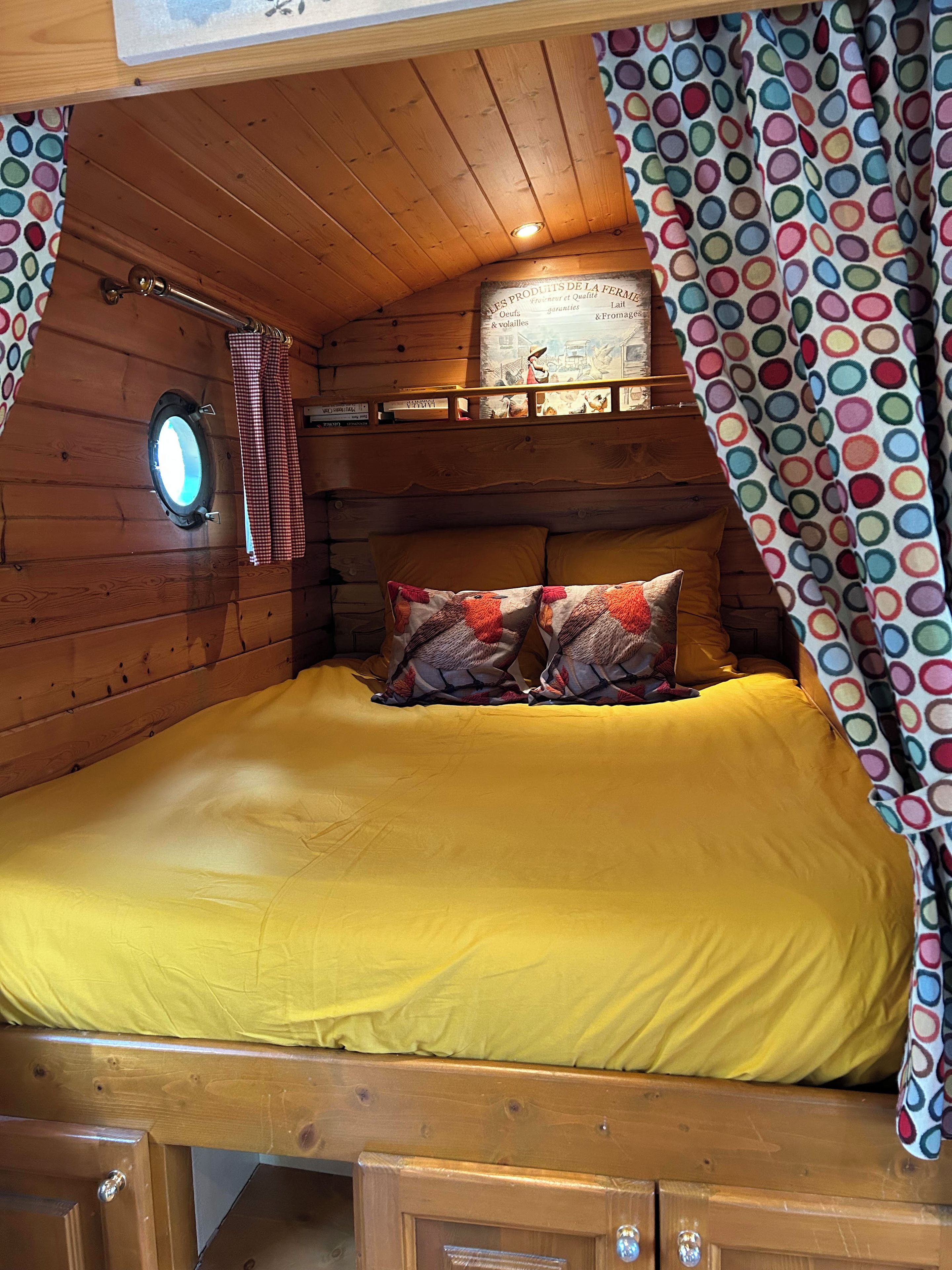 Um quarto acolhedor em estilo cabana, com decoração em madeira, uma cama com roupa de cama amarela e uma janela redonda.
