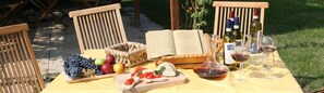 Mesa posta ao ar livre com um livro, frutas, pão e copos de vinho.
