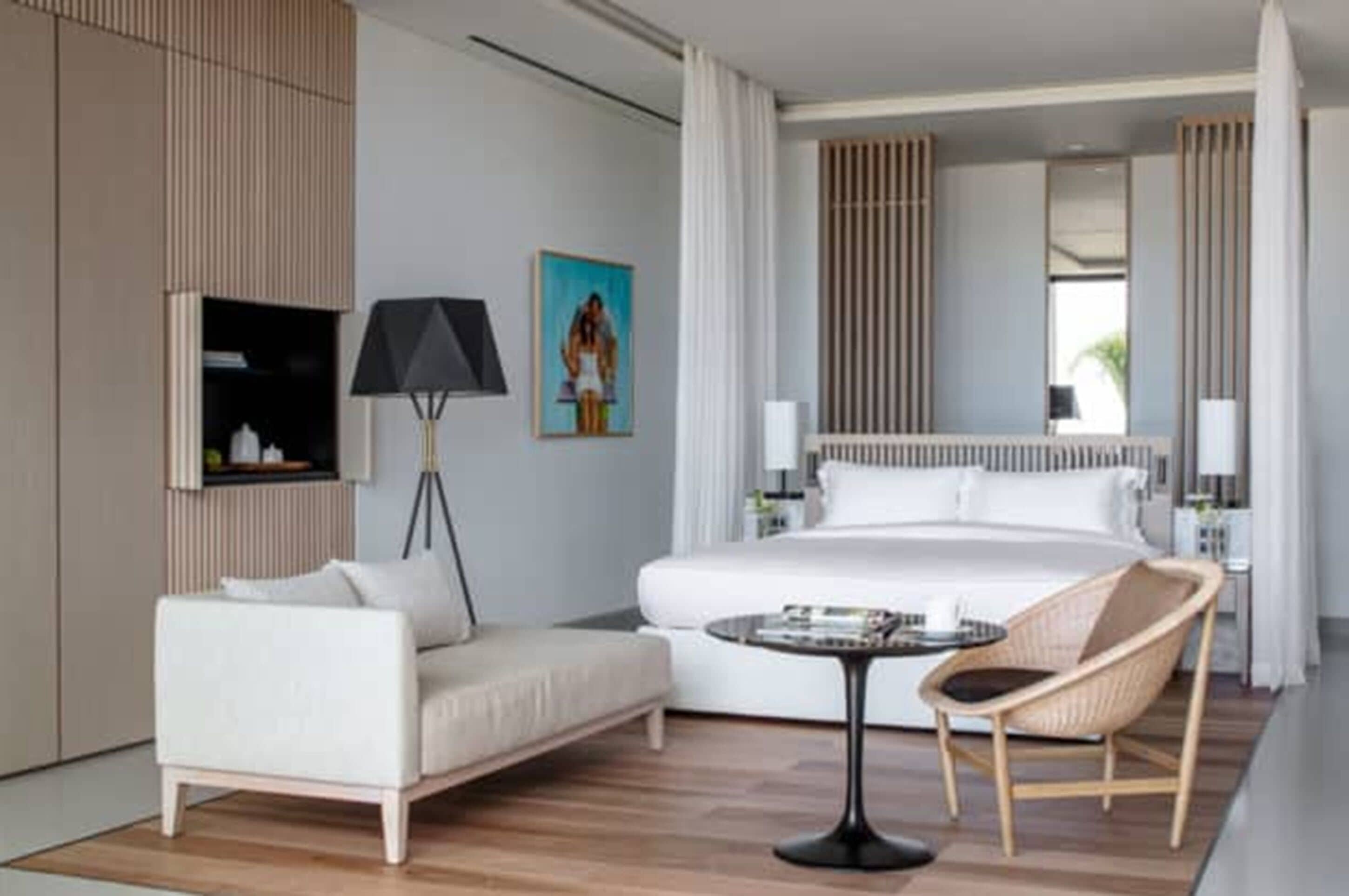 Quarto de hotel moderno com uma cama grande, um sofá, uma poltrona, uma mesinha e um abajur.