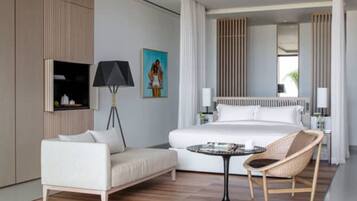 Quarto de hotel moderno com uma cama grande, um sofá, uma poltrona, uma mesinha e um abajur.