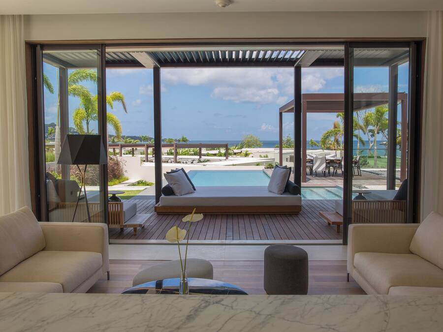 Uma sala de estar moderna com uma grande porta de vidro que dá para uma área de piscina com vista para o oceano.