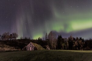 Paisagem rural com uma casa pequena e um campo gramado sob um céu estrelado.
