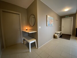 Um corredor com um banco branco, uma mesa pequena com abajur, um espelho fixado na parede e um mapa emoldurado.