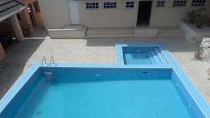 Uma piscina retangular ao ar livre com borda ladrilhada e uma piscina menor adjacente.