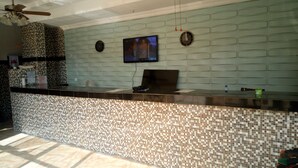 Uma área de recepção com parede revestida de azulejos, uma televisão de tela plana acima do balcão e um ventilador de teto.