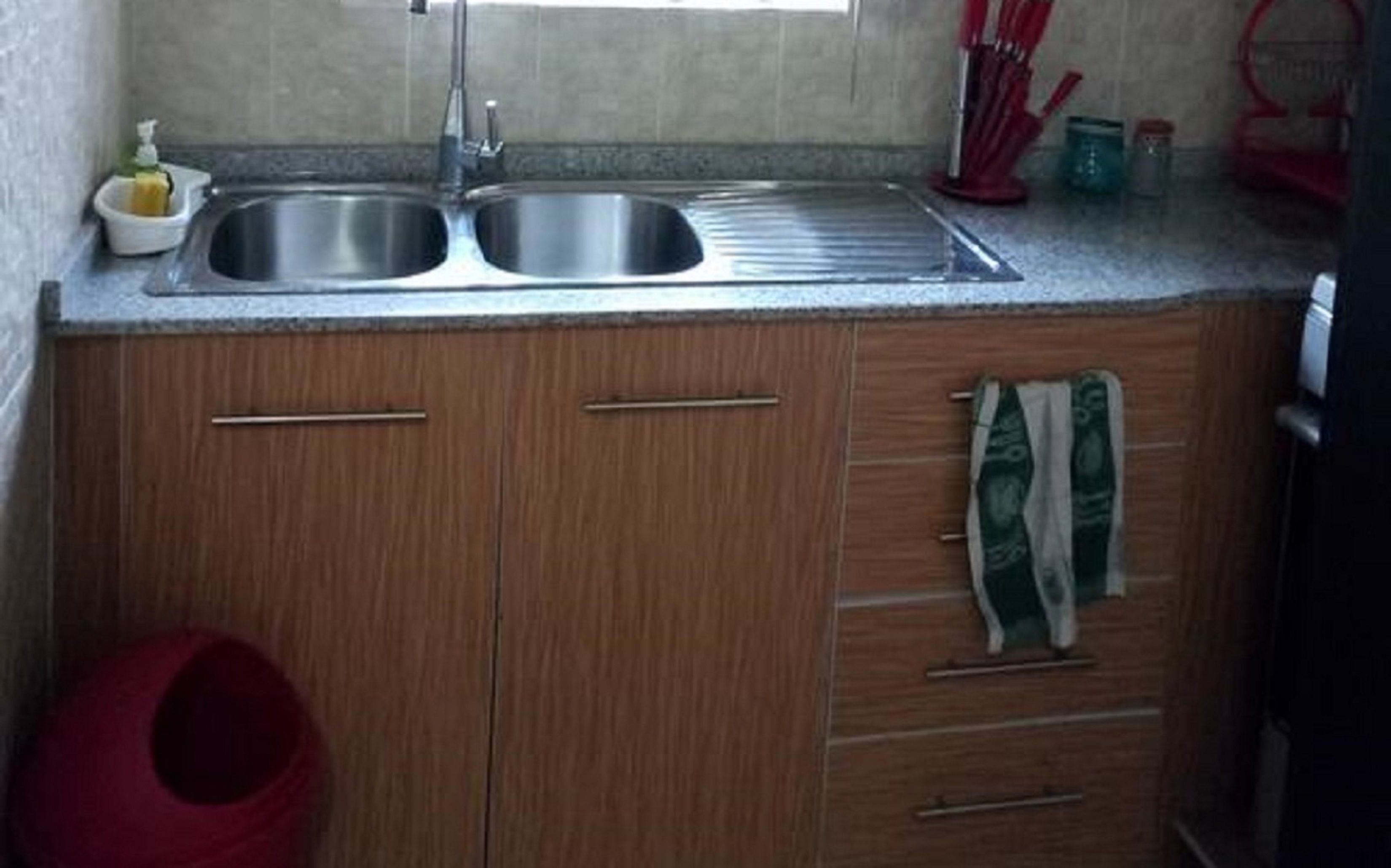 Cozinha com duas pias de aço inoxidável, armários de madeira e uma lixeira vermelha.