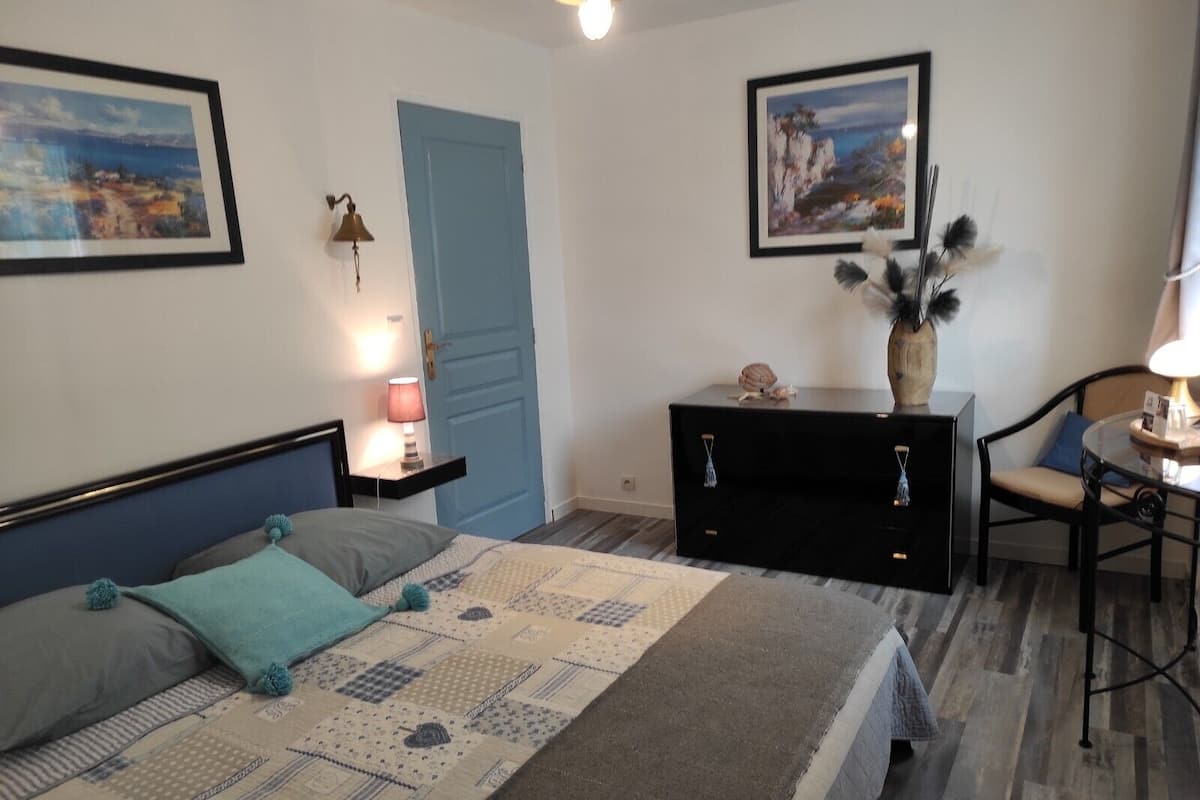 Quarto com cama, mesa de cabeceira, cômoda, cadeira e duas pinturas nas paredes.