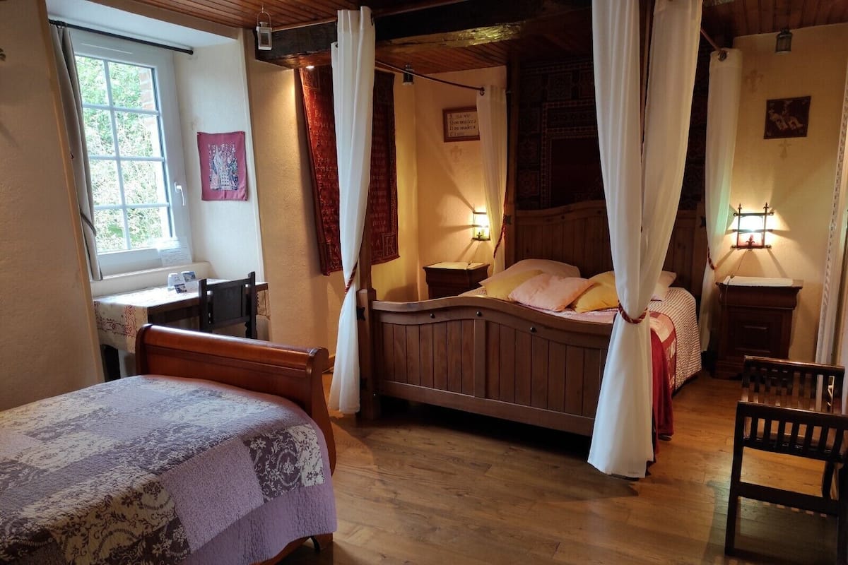 Um quarto aconchegante com uma cama de madeira, uma mesa pequena com uma cadeira e uma janela com cortinas.