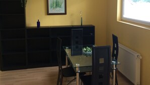 Uma área de refeições com mesa e cadeiras de vidro, um armário preto, um quadro na parede e uma janela com vista.