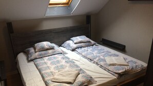 Uma cama de solteiro com roupa de cama floral, cabeceira de madeira e um claraboia acima.