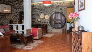 Um interior rústico com paredes de pedra, um barril de madeira e um abajur vermelho pendurado.