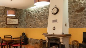 Uma sala de estar acolhedora, com parede de pedra, lareira, mesa de jantar com cadeiras e um candeeiro pendente.