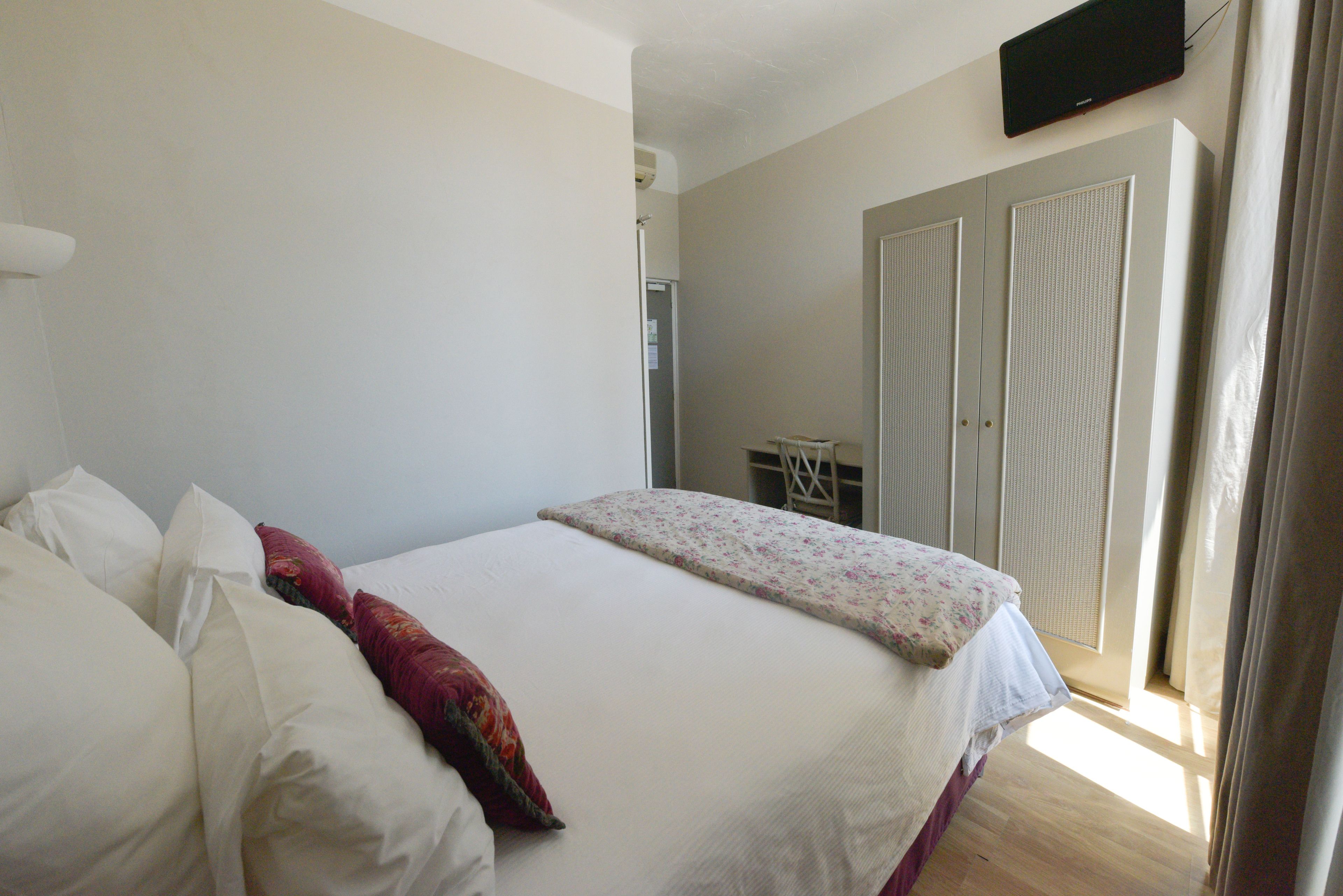 Quarto com cama, almofadas, televisão na parede e porta para outro cômodo.