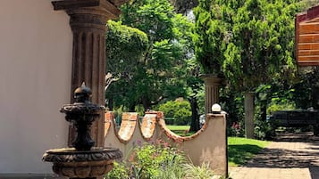 Um caminho no jardim com uma fonte, um muro de tijolos e vegetação exuberante.