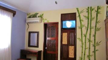 Quarto com porta de madeira, televisão fixada na parede e papel de parede com padrão de bambu.