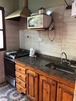 Uma cozinha com fogão, micro-ondas, pia e armários de madeira.