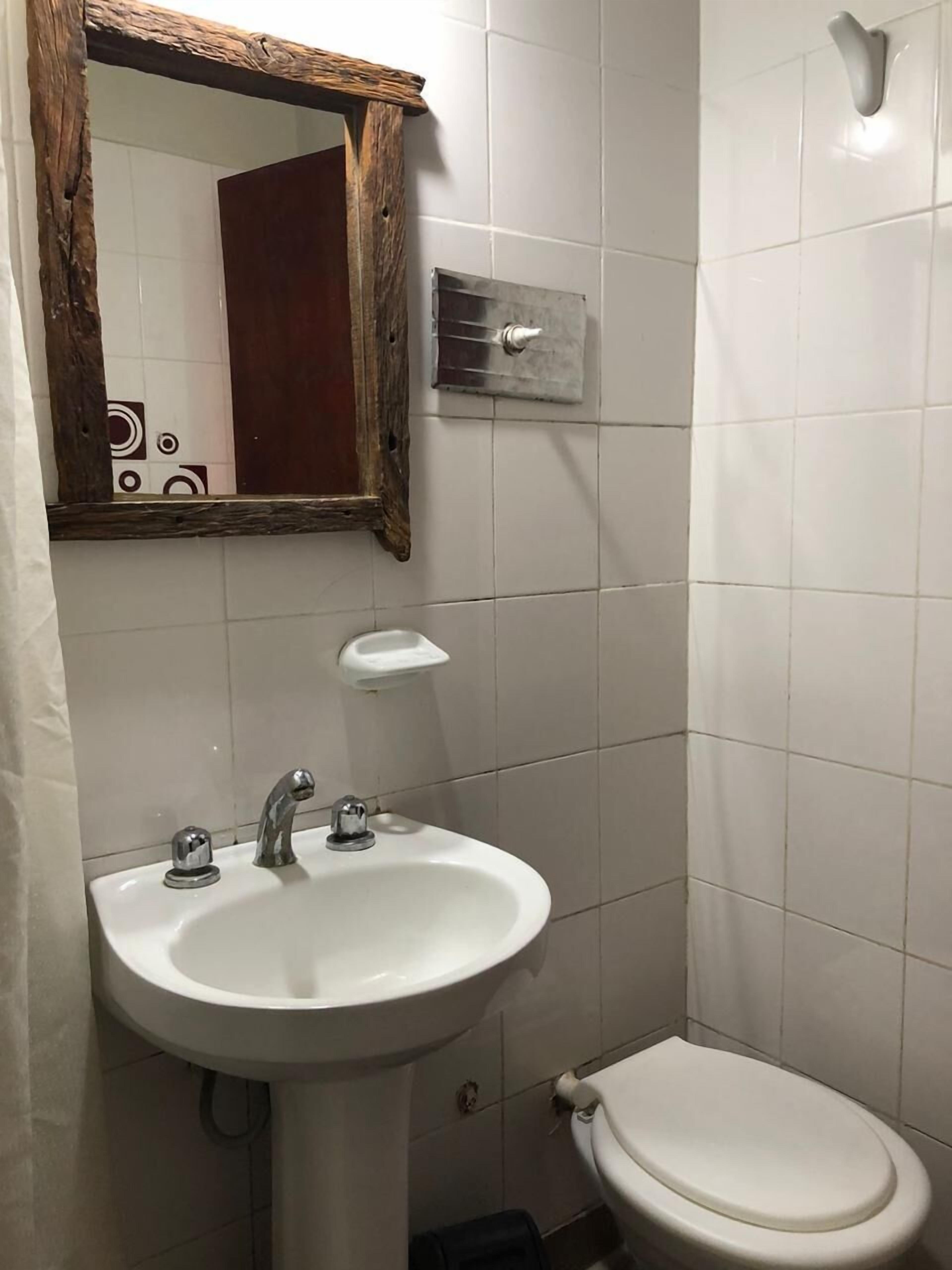 Casa de banho com lavatório branco, espelho e sanita.