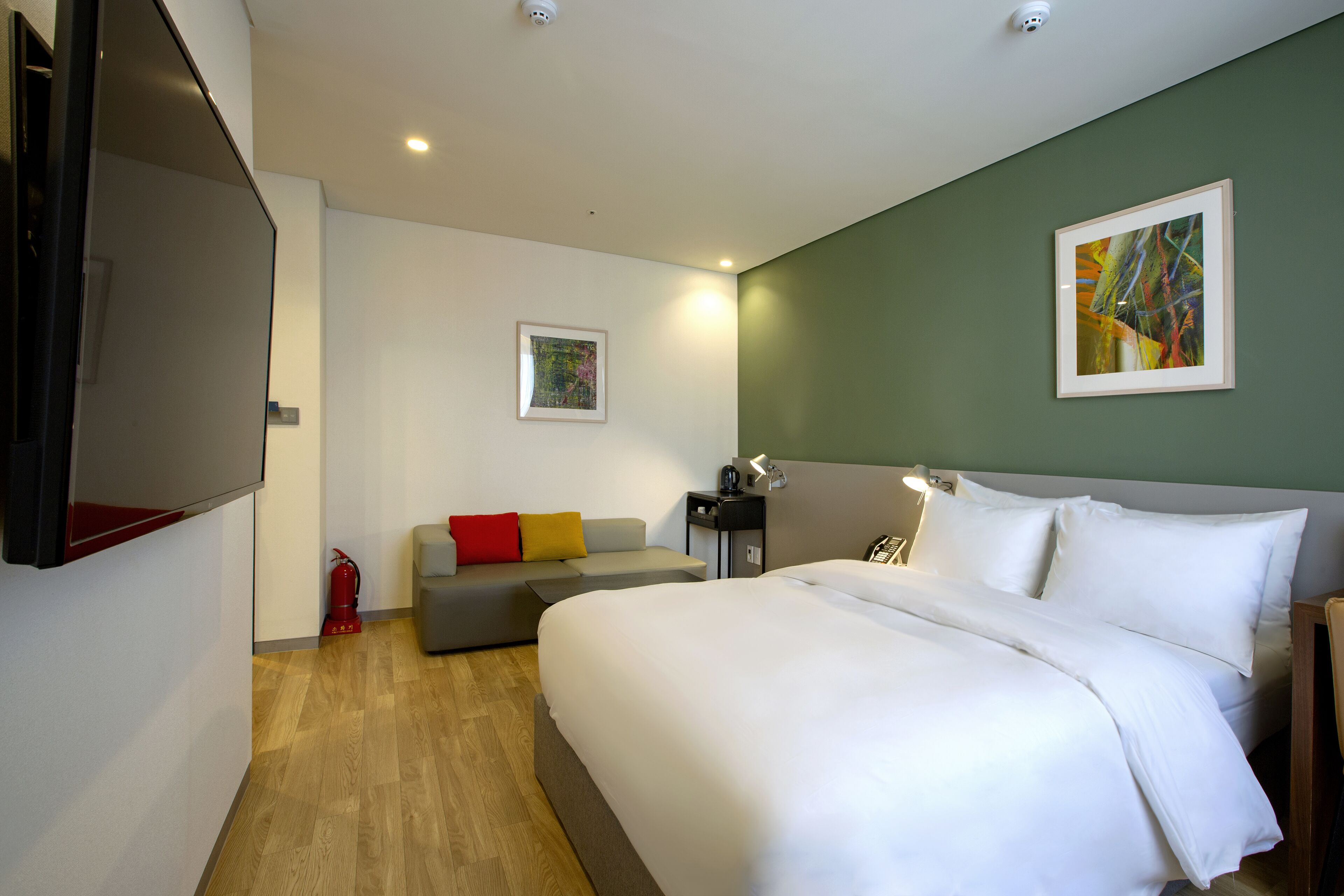 Quarto de hotel moderno com uma cama grande, um sofá, uma mesinha e uma televisão.