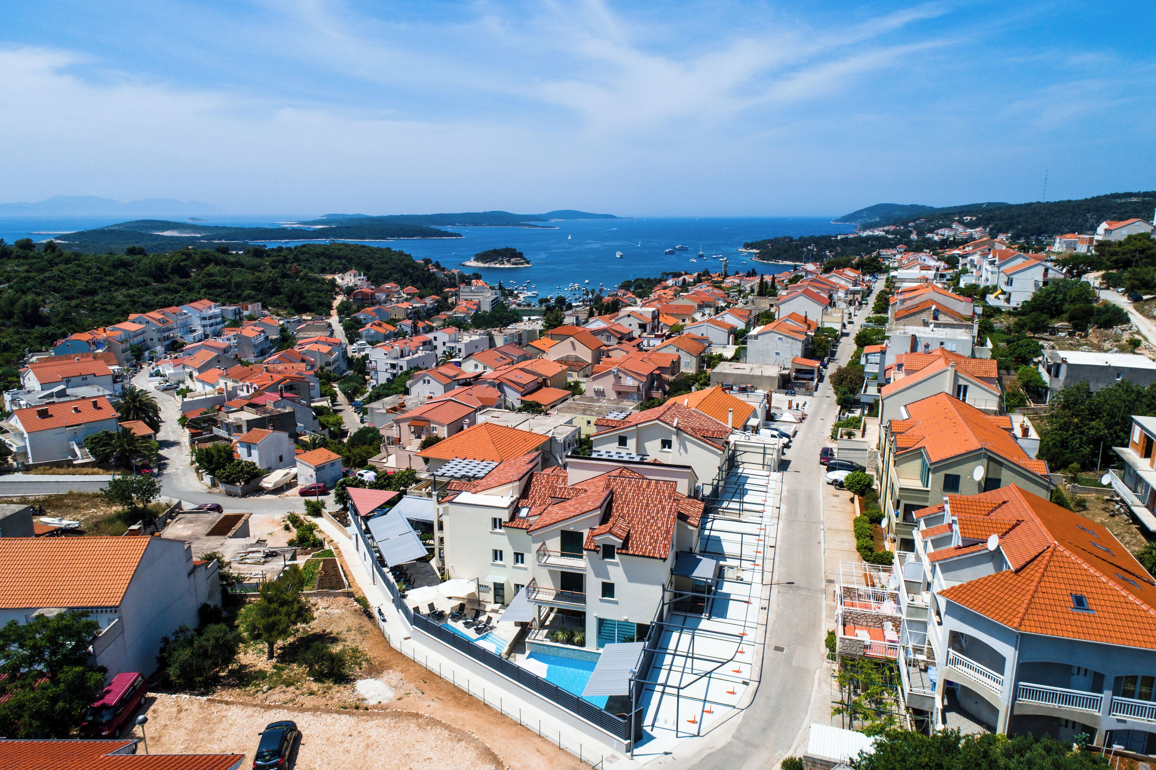 Uma área residencial costeira com casas de telhado vermelho, piscina e vista clara para o mar.