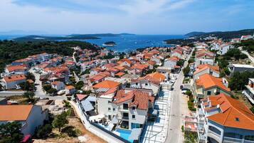 Uma área residencial costeira com casas de telhado vermelho, piscina e vista clara para o mar.