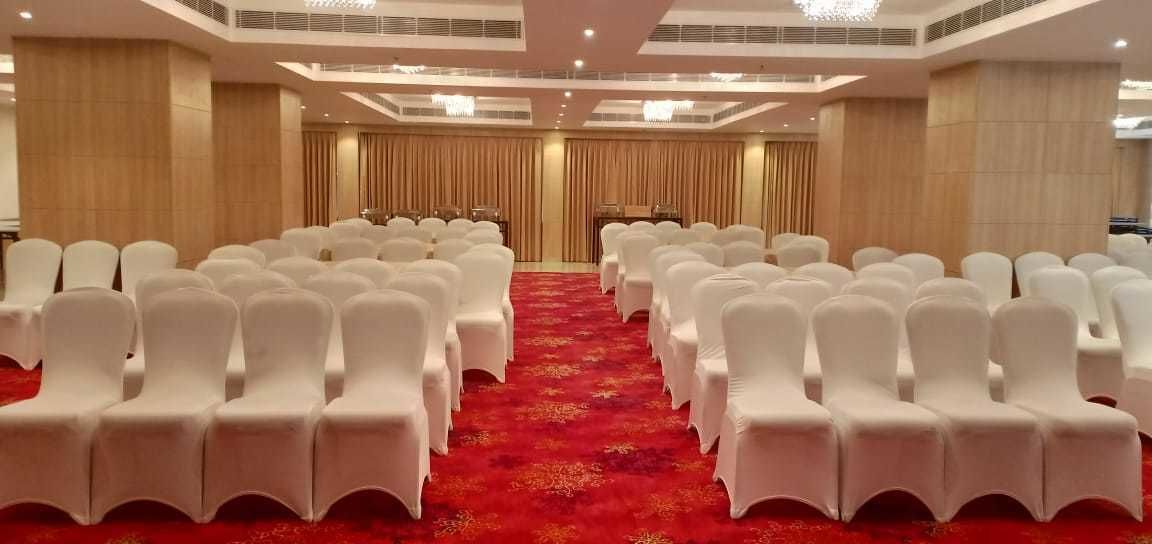 Uma sala de conferências com fileiras de cadeiras brancas, um tapete vermelho e um pódio na frente.